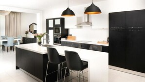 Cozinha moderna com armários pretos, bancada branca e duas luminárias pendentes.