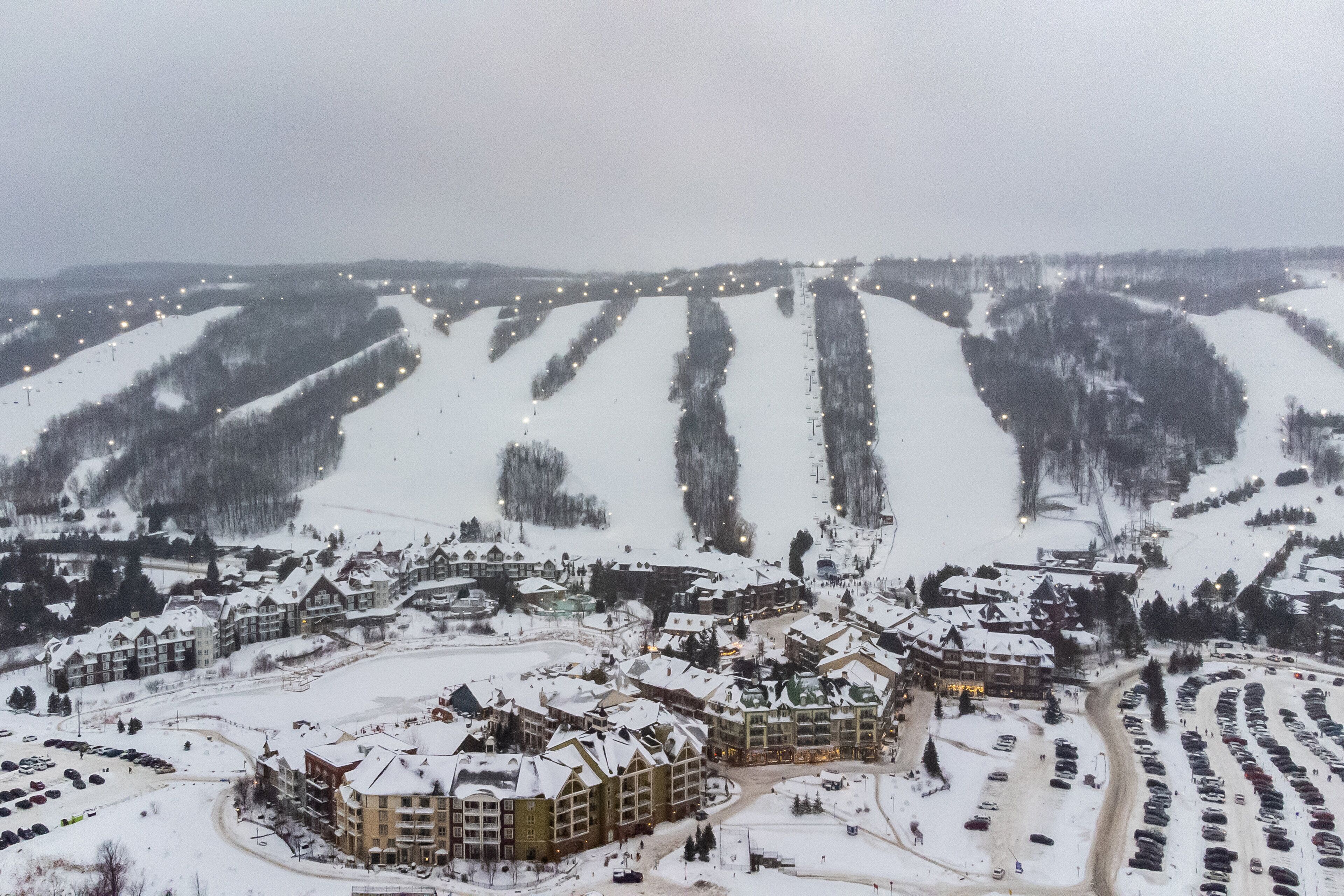 Estância de esqui coberta de neve, com vários edifícios, áreas de estacionamento e pistas de esqui.