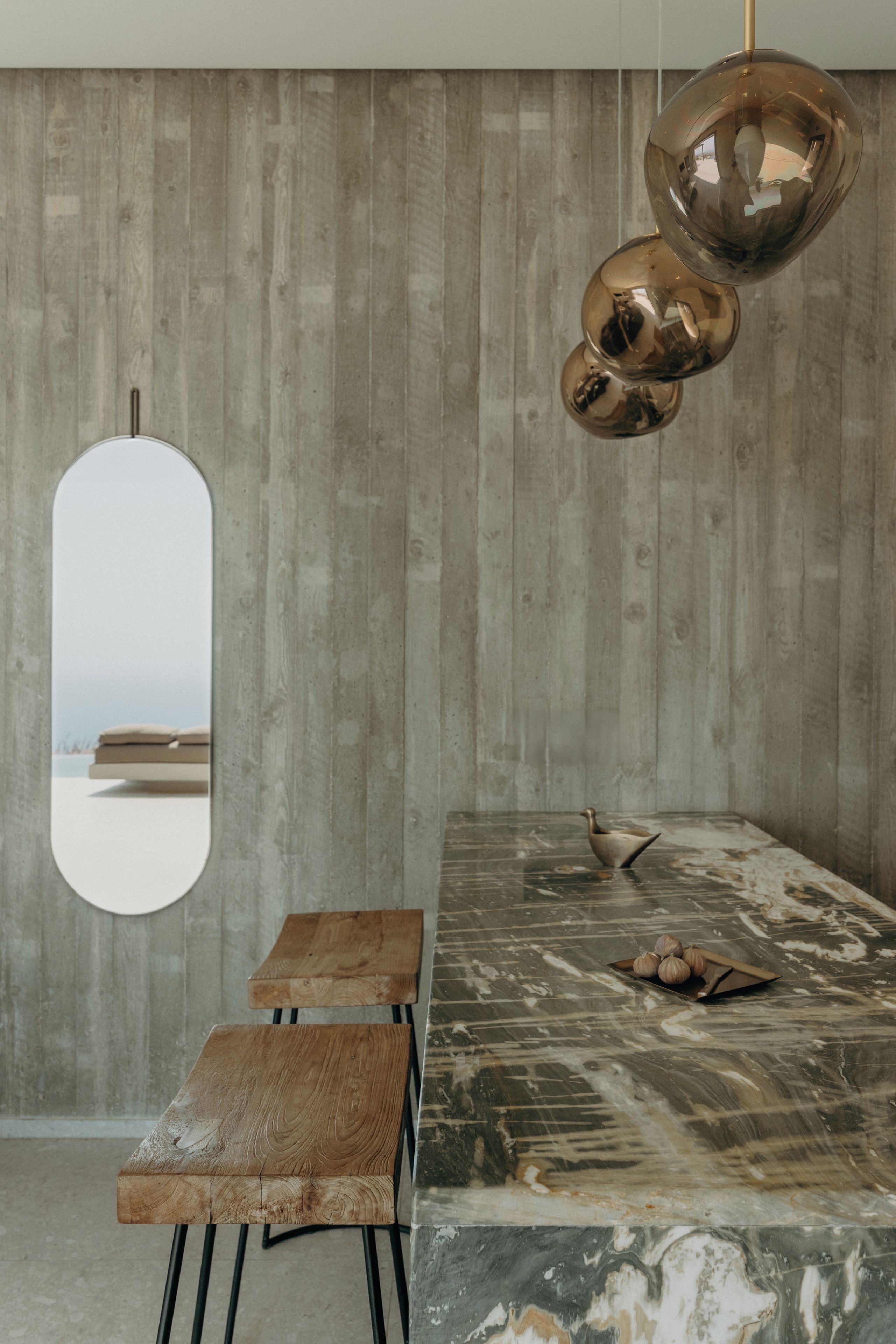 Decoração moderna com um banco de madeira, uma mesa de mármore e um lustre esférico pendurado.
