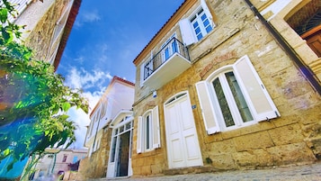 Uma rua estreita com edifícios de pedra, grades brancas e uma varanda com guarda-corpo de metal.