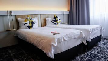 Quarto de hotel com duas camas, cabeceira, mesa de cabeceira e carpete estampado.