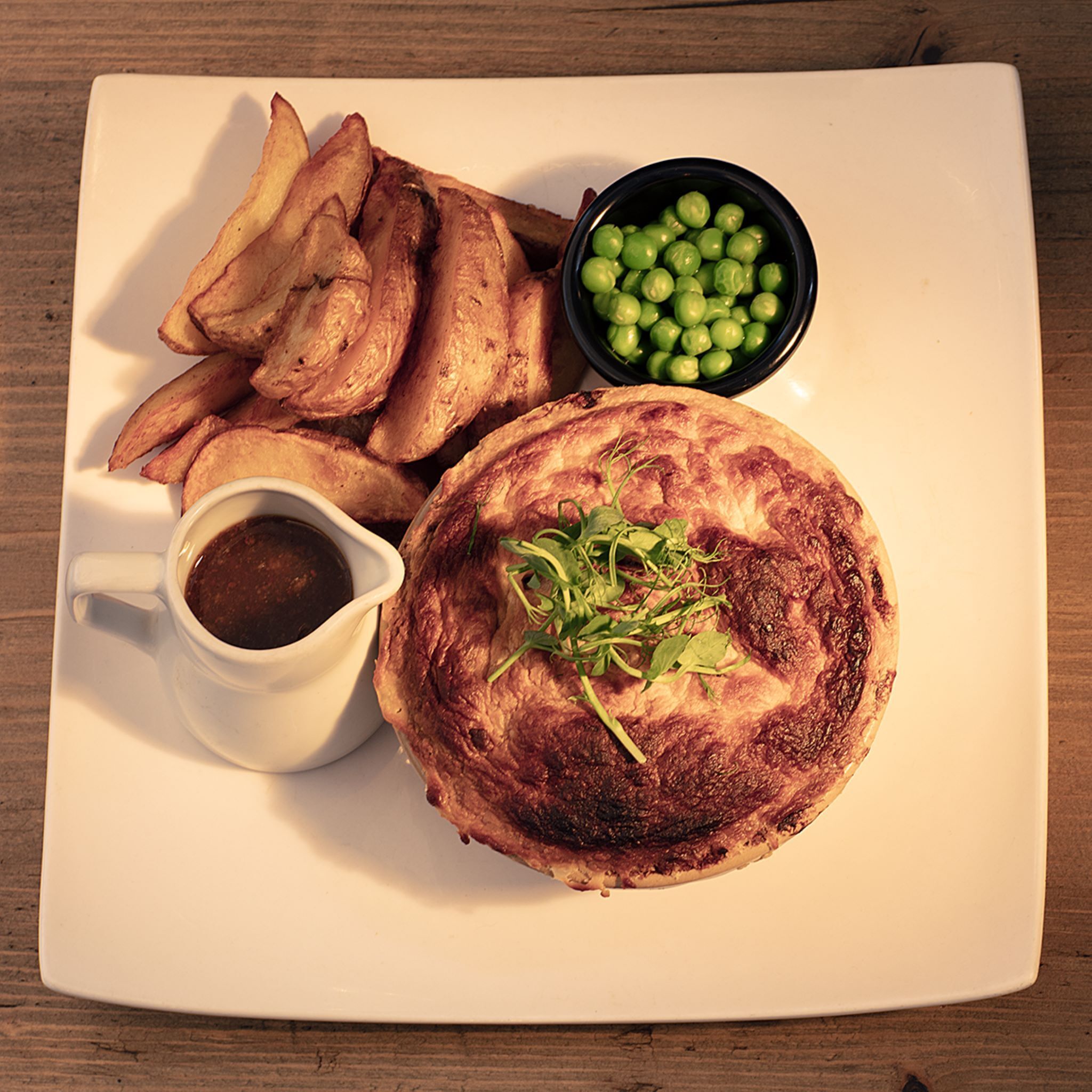 Um prato com pudim Yorkshire, batatas assadas, ervilhas e molho gravy.