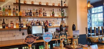 Uma área de bar com prateleiras de garrafas de bebidas, um monitor de computador e torneiras de chopp com nomes de marcas.