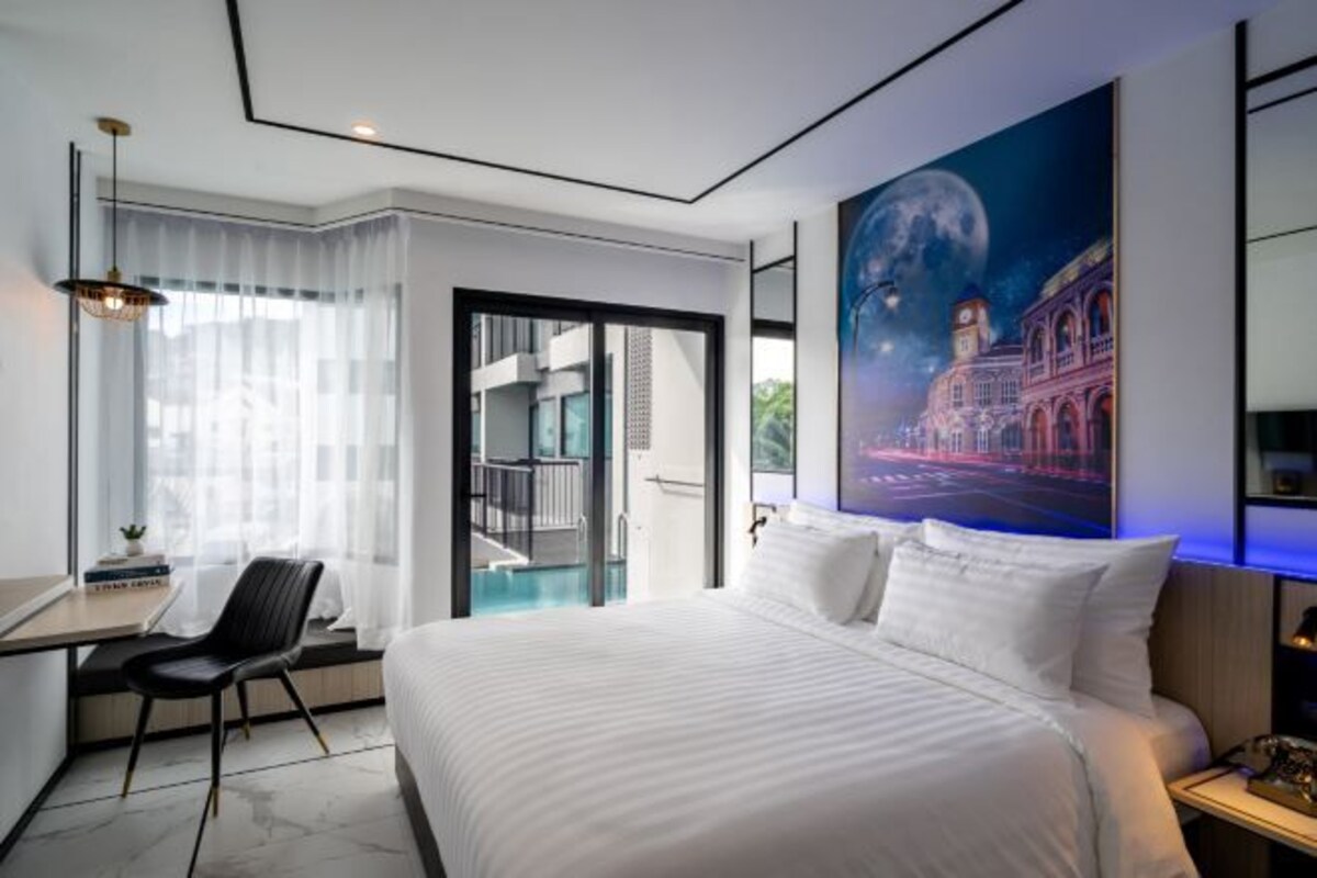 Quarto de hotel moderno com uma cama grande, uma escrivaninha com cadeira e uma varanda com vista para um edifício.