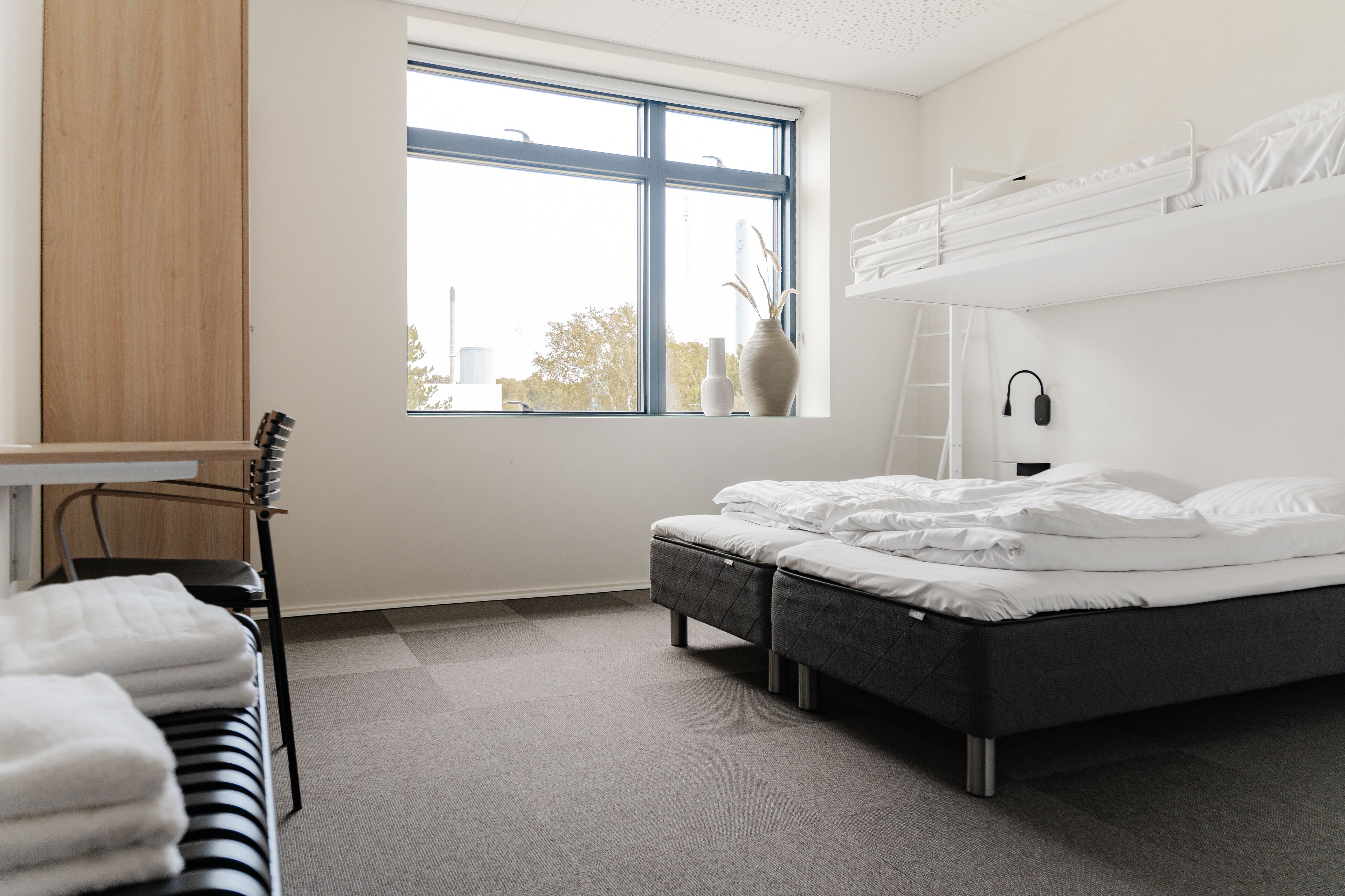 Quarto moderno com beliche, escrivaninha com teclado, um violão e janela com vista para árvores.