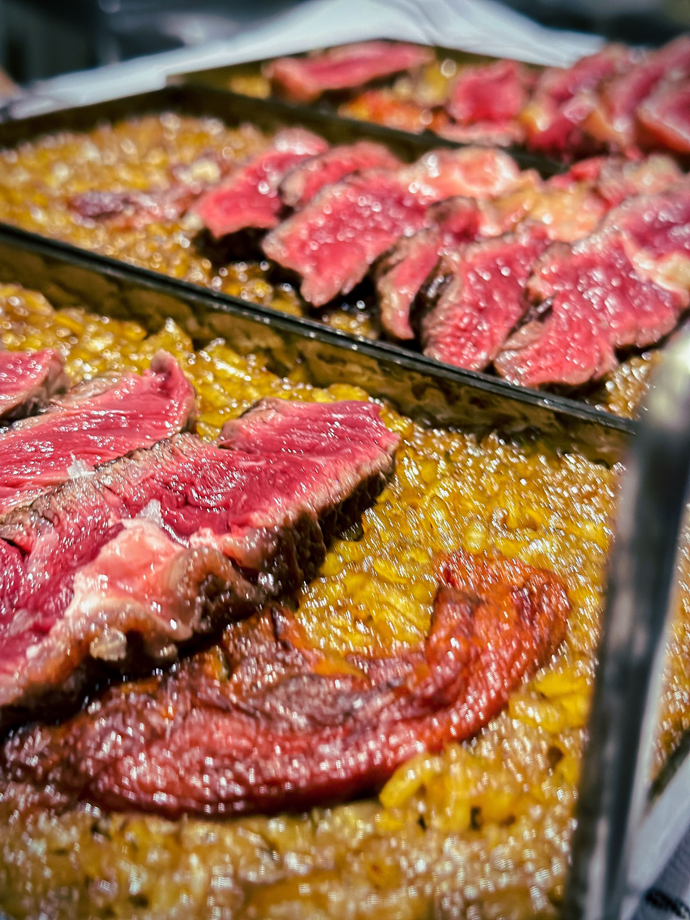 Close-up de carne cozinhada com superfície brilhante e caramelizada, provavelmente numa frigideira.