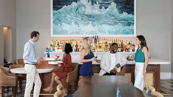 Uma área de bar com uma grande pintura abstrata, um balcão com diversos frascos e um espaço de estar com cadeiras e uma mesa.
