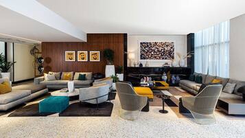 Uma sala de estar moderna com um sofá, uma mesa de centro e duas poltronas decorativas. Há uma lareira e um grande quadro abstrato na parede.