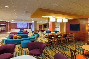 Um hall de hotel com áreas de estar, balcão de recepção, uma tela de televisão e um espaço de recreação infantil.