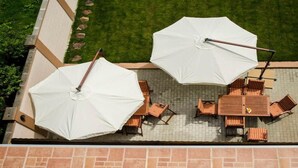 Pátio externo com duas grandes ombrelhas brancas, uma mesa de madeira e cadeiras combinando.