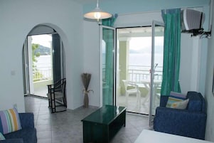 Quarto com sofá, um banquinho, mesa e vista para o mar através de uma porta de vidro.