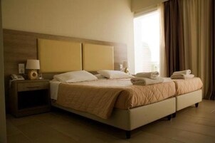 Quarto de hotel com uma cama grande, duas mesas de cabeceira, uma luminária e uma janela com cortinas.