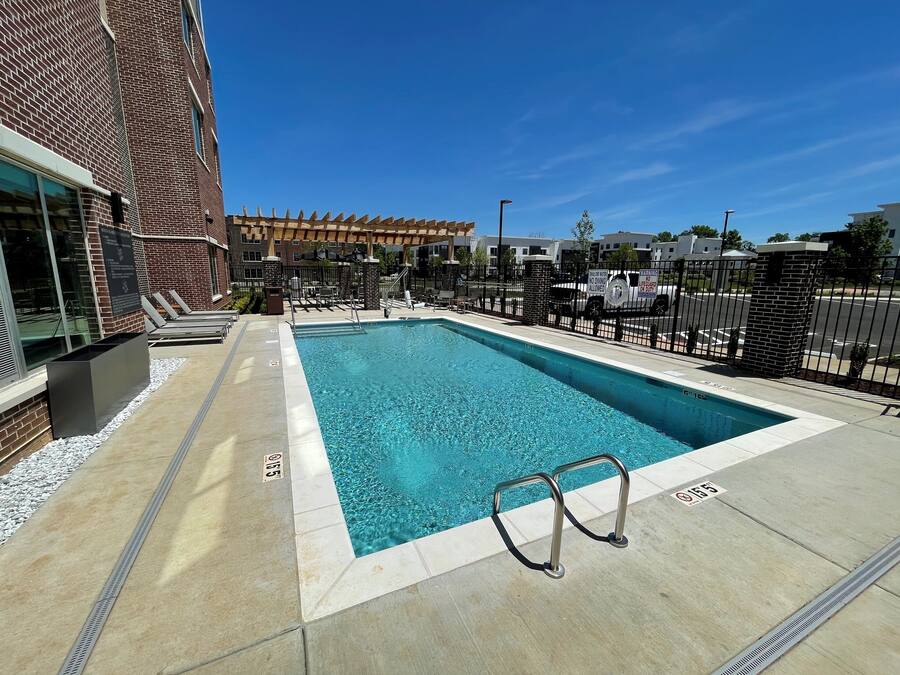Piscina retangular ao ar livre com água azul cristalina, rodeada por uma cerca de metal preto.