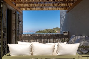 Varanda com vista para o mar, uma parede de pedra e uma mesa com almofadas.