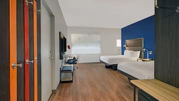 Quarto de hotel com duas camas, uma escrivaninha, uma cadeira, uma televisão e uma janela com vista para o céu.