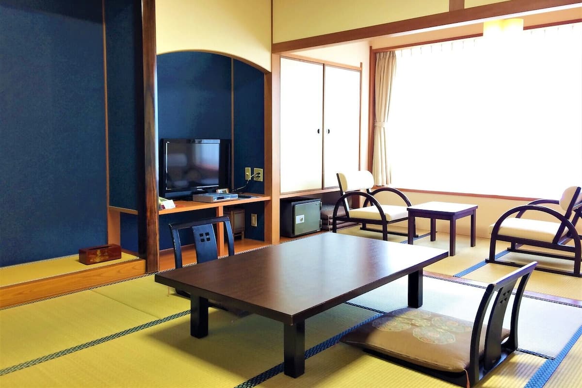 Um quarto tradicional com esteiras de tatame, televisão, assentos e vista para o exterior.