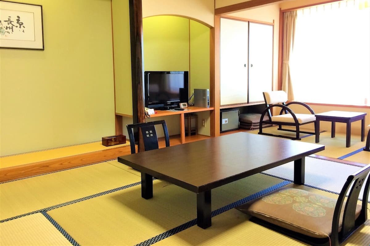 Um quarto em estilo japonês tradicional, com tatames, uma mesa baixa, uma televisão e uma cadeira.