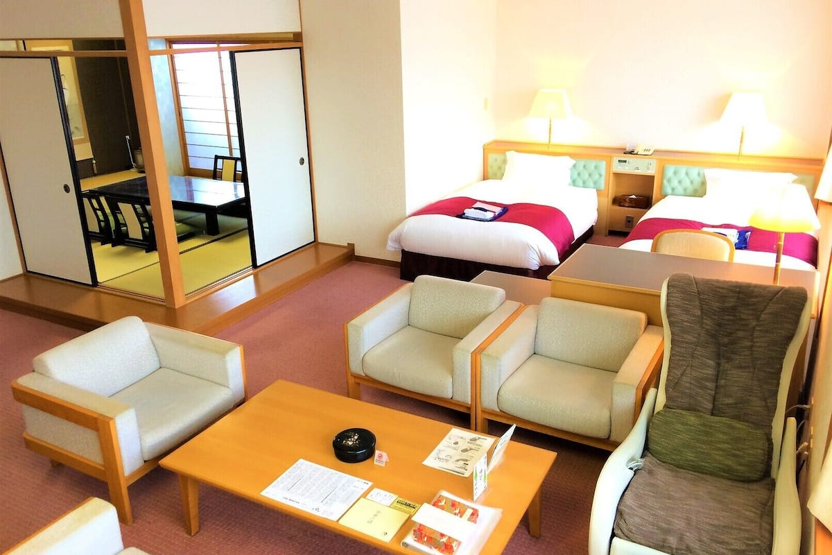 Quarto de hotel com cama, duas mesas de cabeceira, escrivaninha, poltrona e sofá.