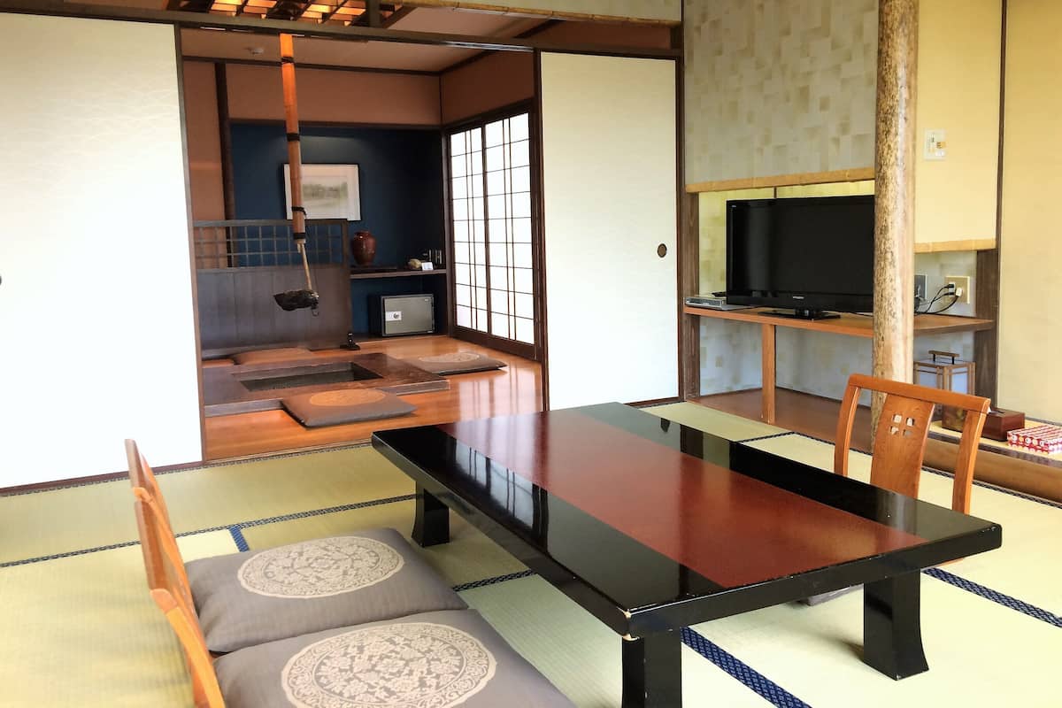 Um quarto japonês tradicional com chão de tatame, uma mesa baixa e uma televisão sobre um suporte de madeira.