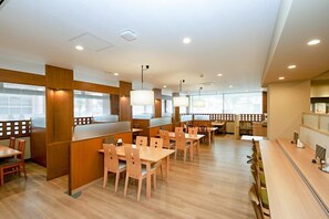 Uma sala de jantar ampla com mesas e cadeiras de madeira, um balcão e vista para o exterior.