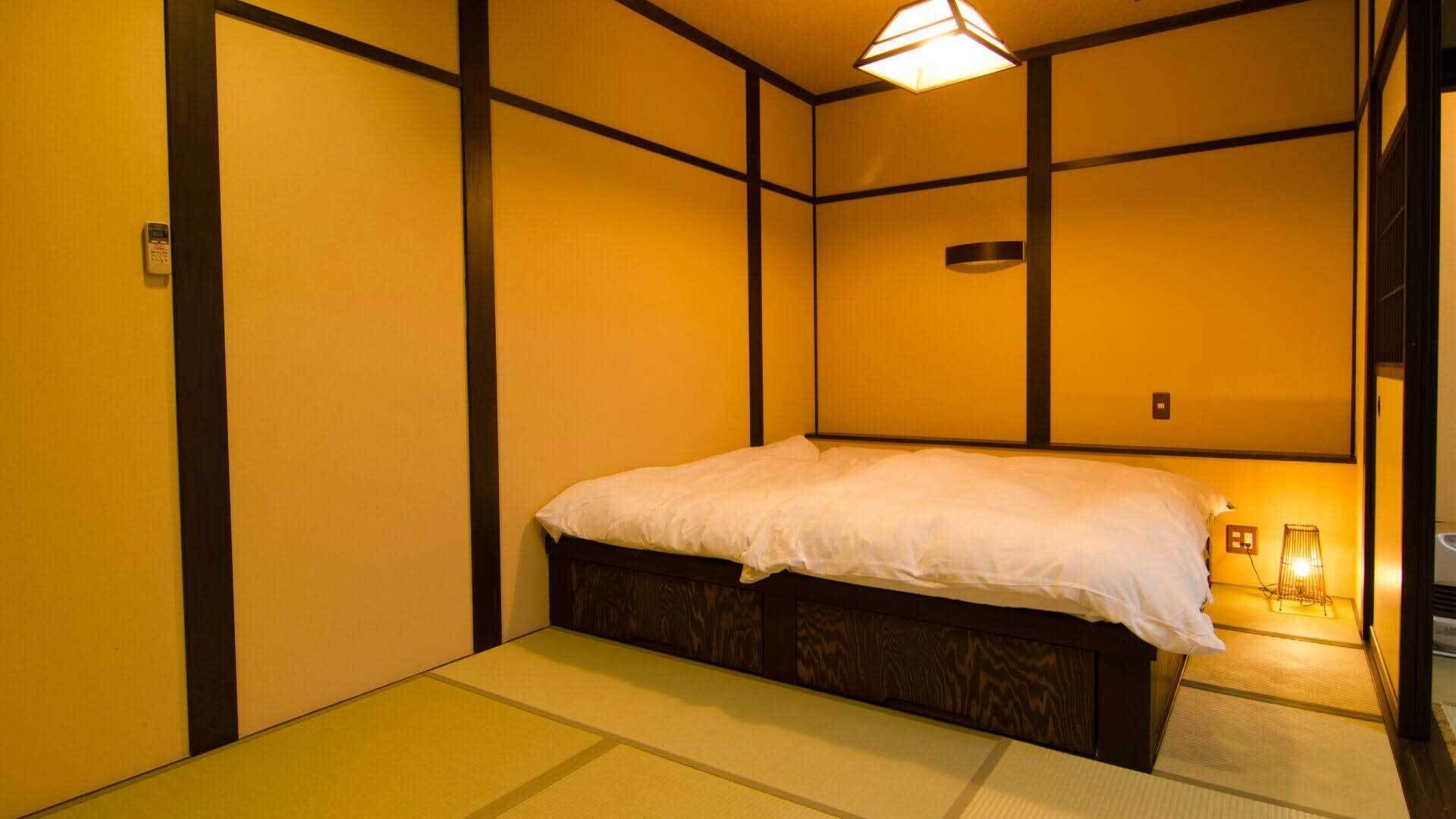 Quarto tradicional japonês com tatames, uma cama e porta de shoji.