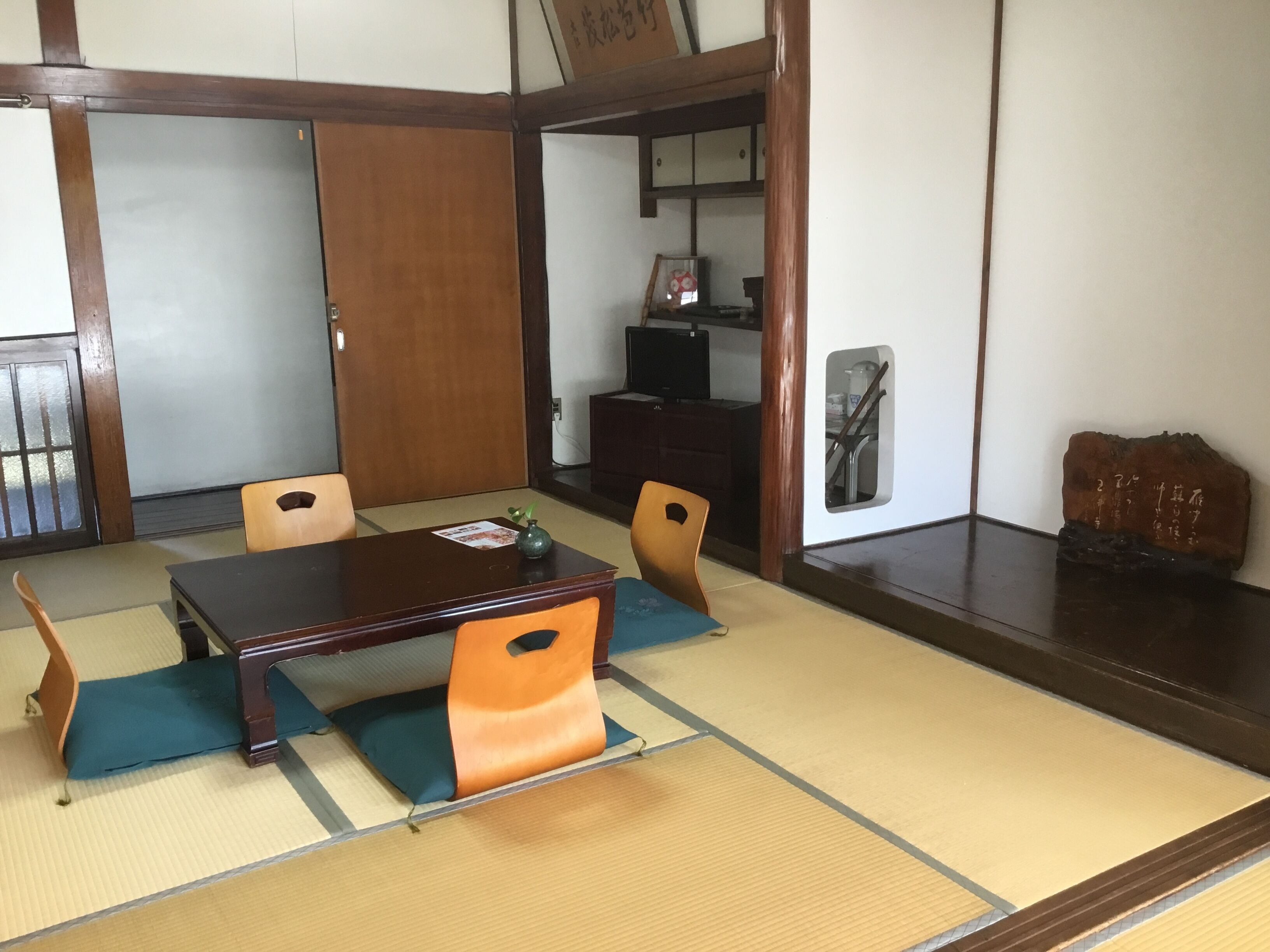 Quarto tradicional japonês com piso de tatame, uma mesa baixa e cadeiras de madeira.