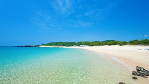 Uma praia com águas turquesa cristalinas, areia dourada e colinas verdes ao fundo.