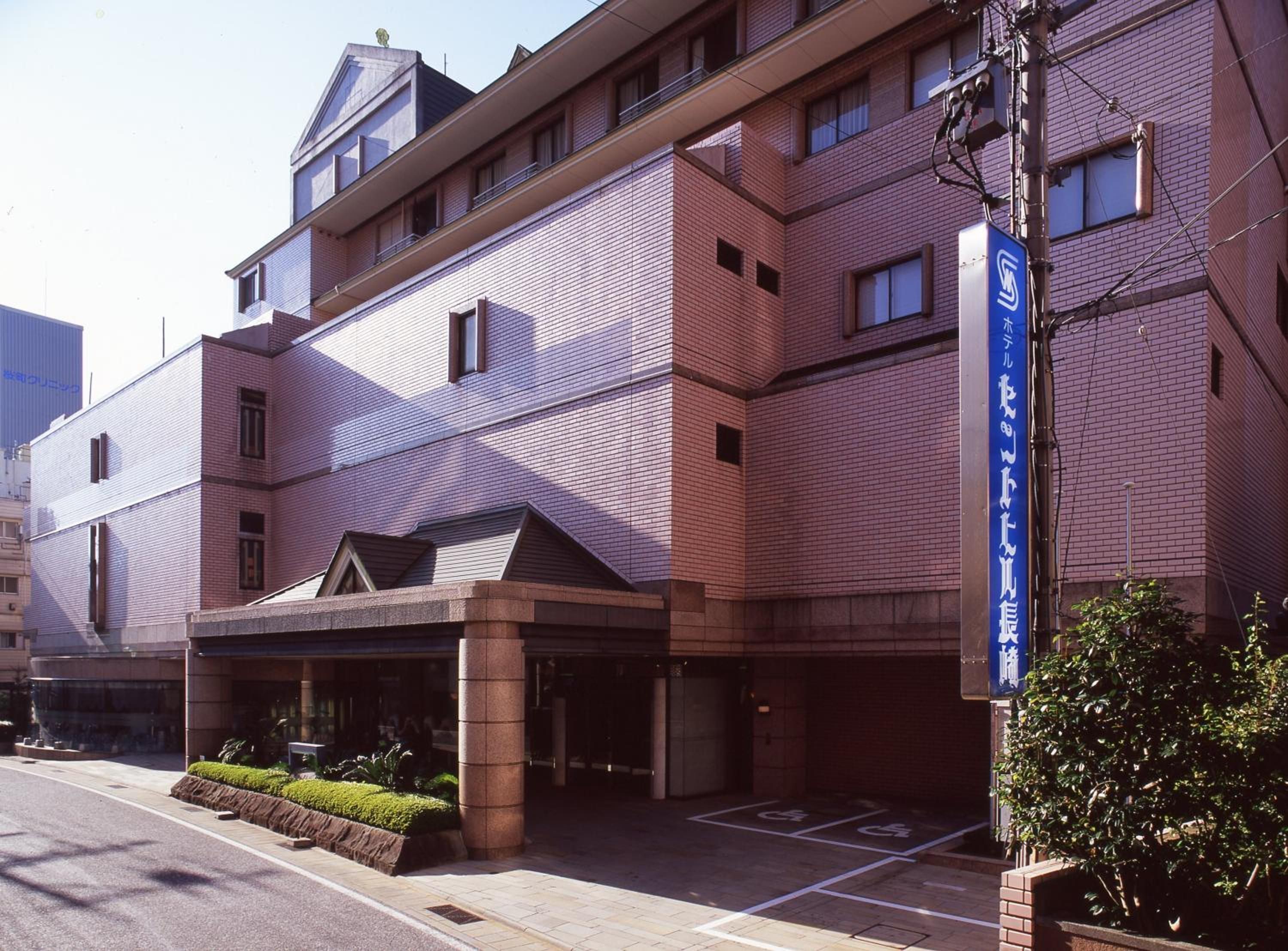Hotel de vários andares com fachada de tijolos, entrada visível e área de estacionamento identificada com o símbolo de acessibilidade.