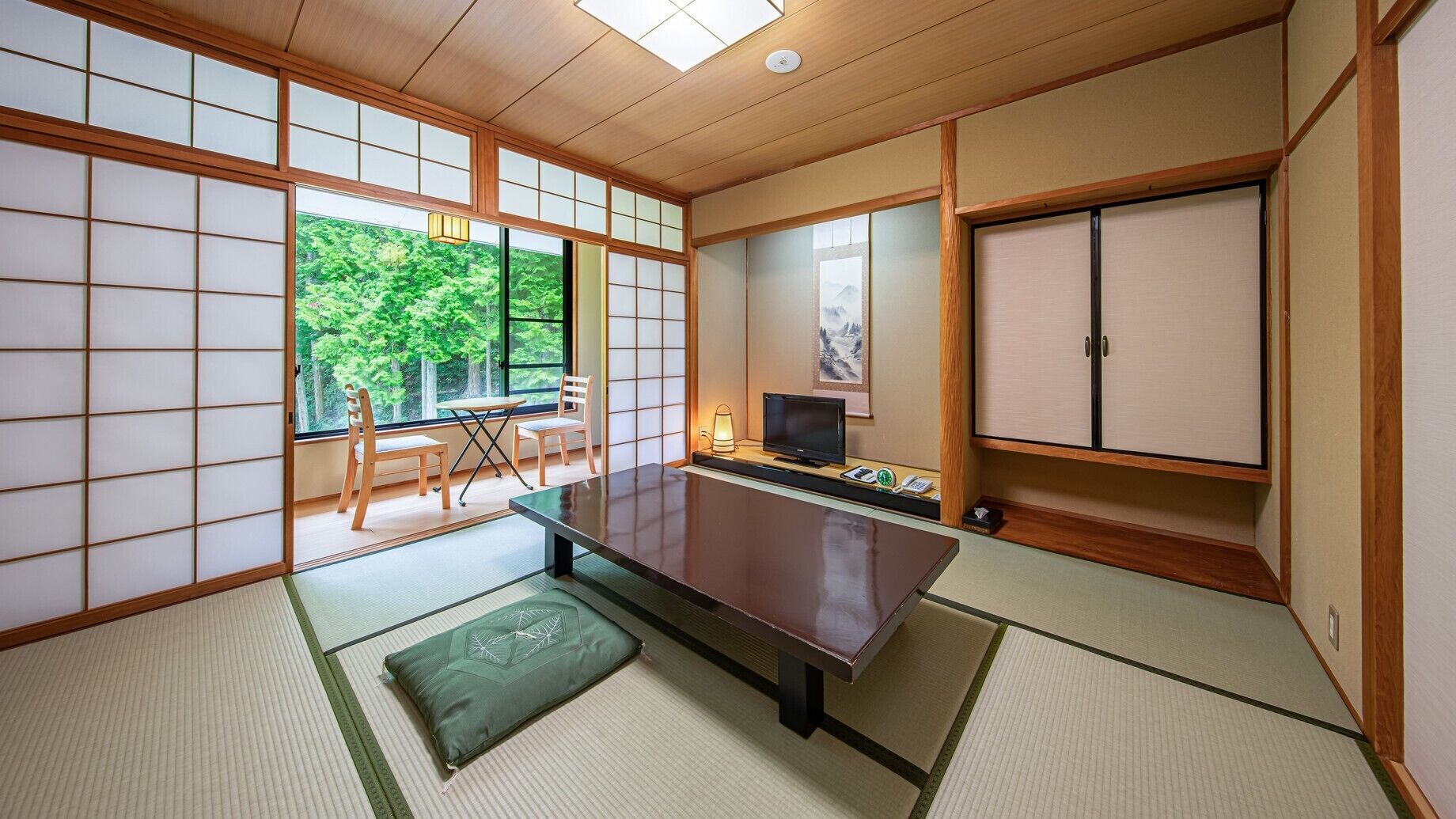 Um quarto japonês tradicional com tatames, uma mesa baixa, cadeiras, televisão e portas deslizantes.