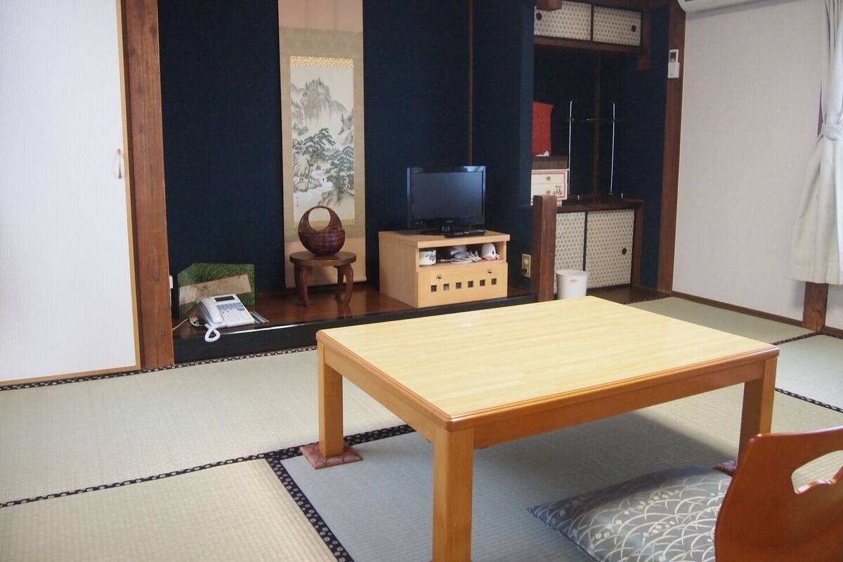 Um quarto japonês tradicional com tatames, uma mesa baixa, uma televisão e um armário com espaço para guardar objetos.