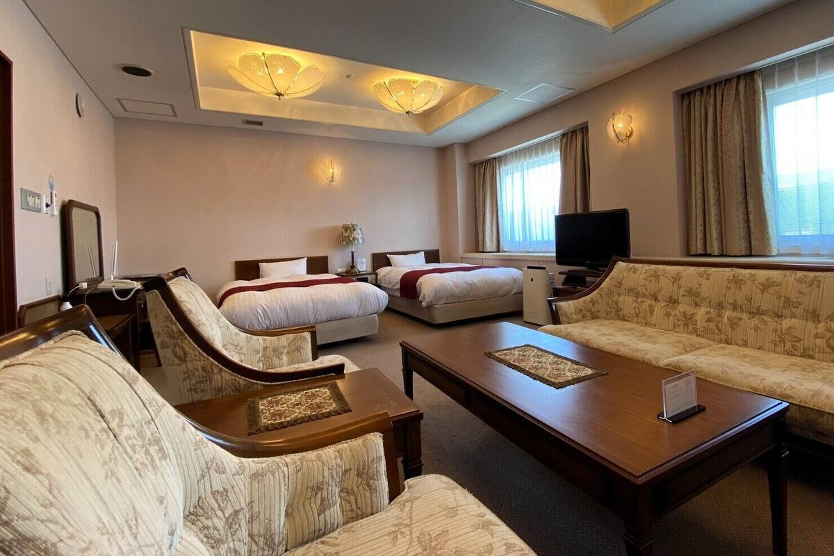 Quarto de hotel com duas camas, um sofá, uma mesa de centro e uma televisão.