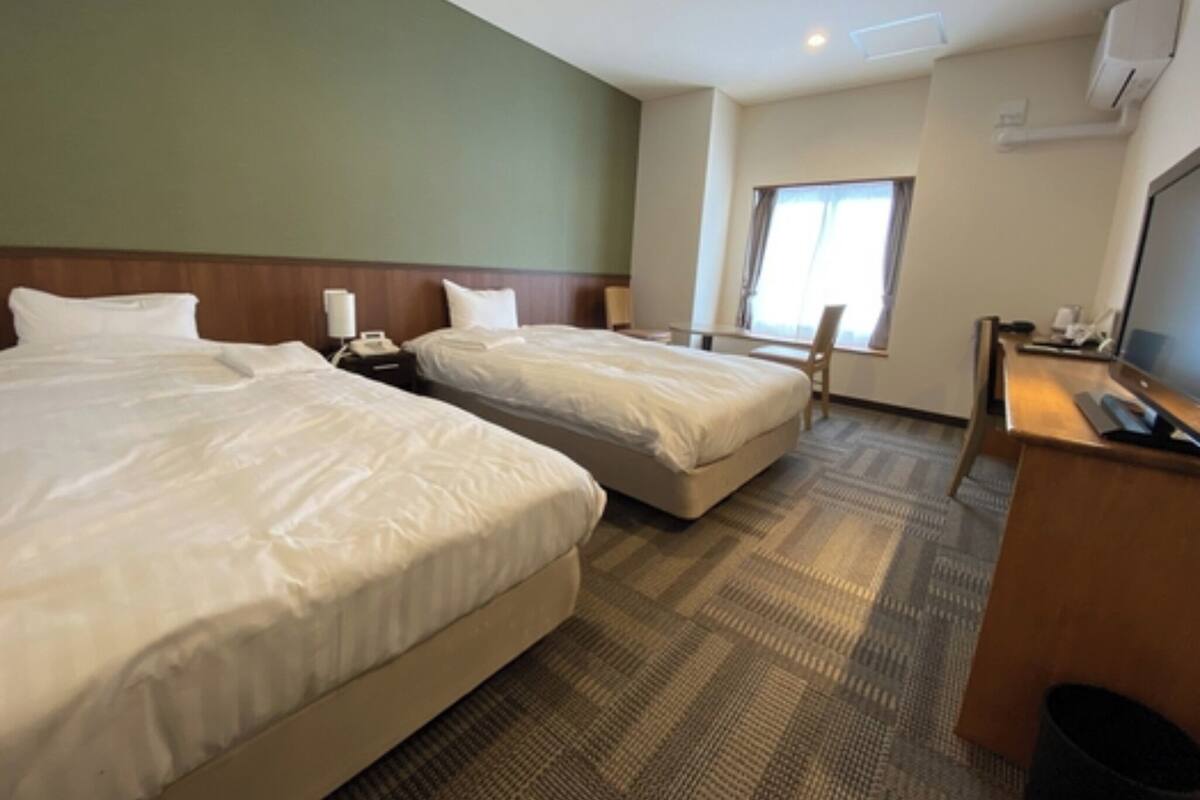 Quarto de hotel com duas camas, uma escrivaninha, uma cadeira, uma televisão e uma janela.