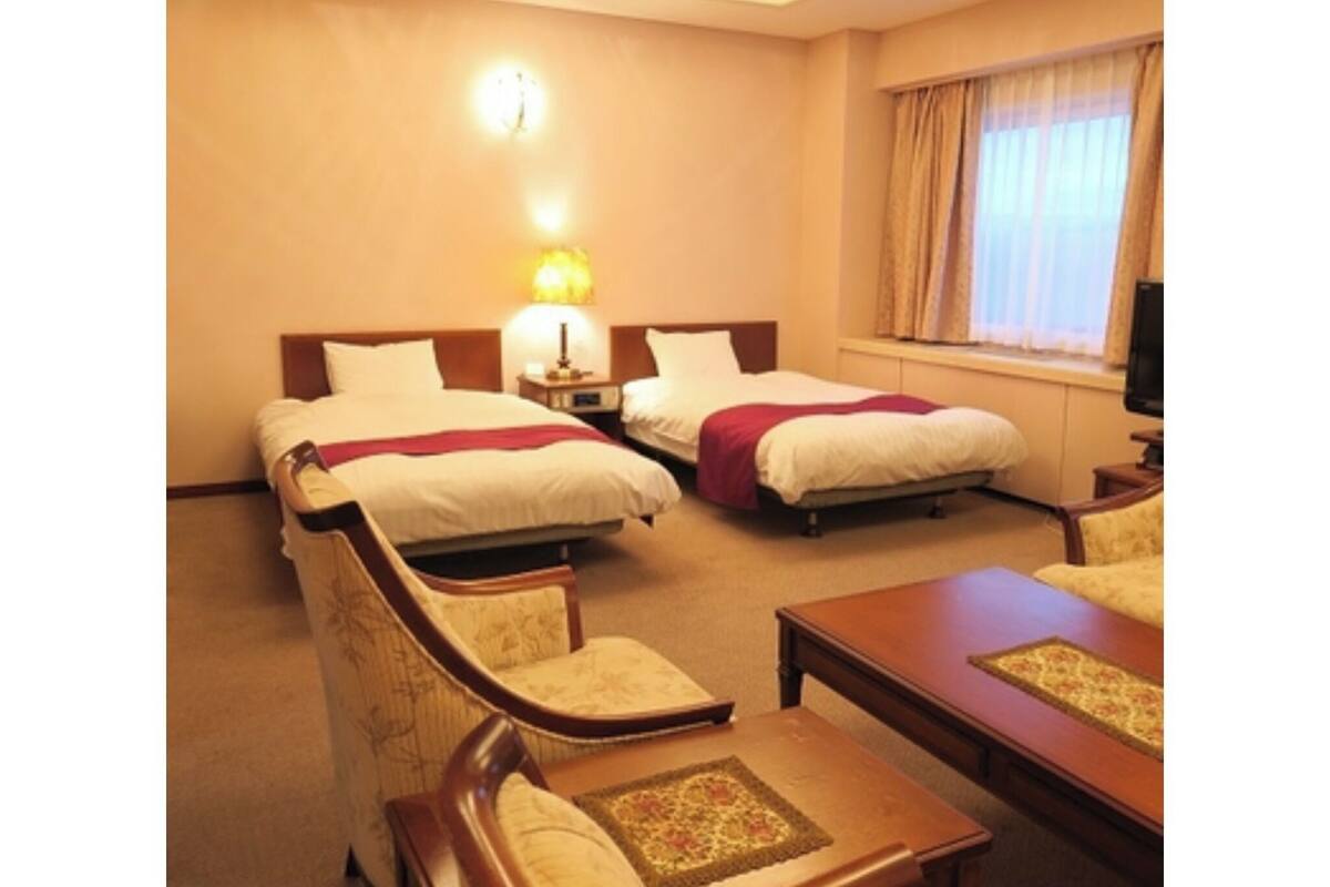 Quarto de hotel com duas camas, um sofá, uma mesa, um abajur e uma televisão.