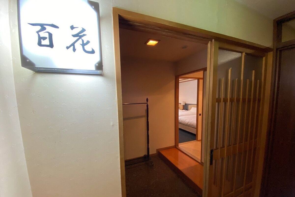 Quarto de hotel com uma cama, uma porta deslizante de madeira e um aviso com caracteres japoneses.