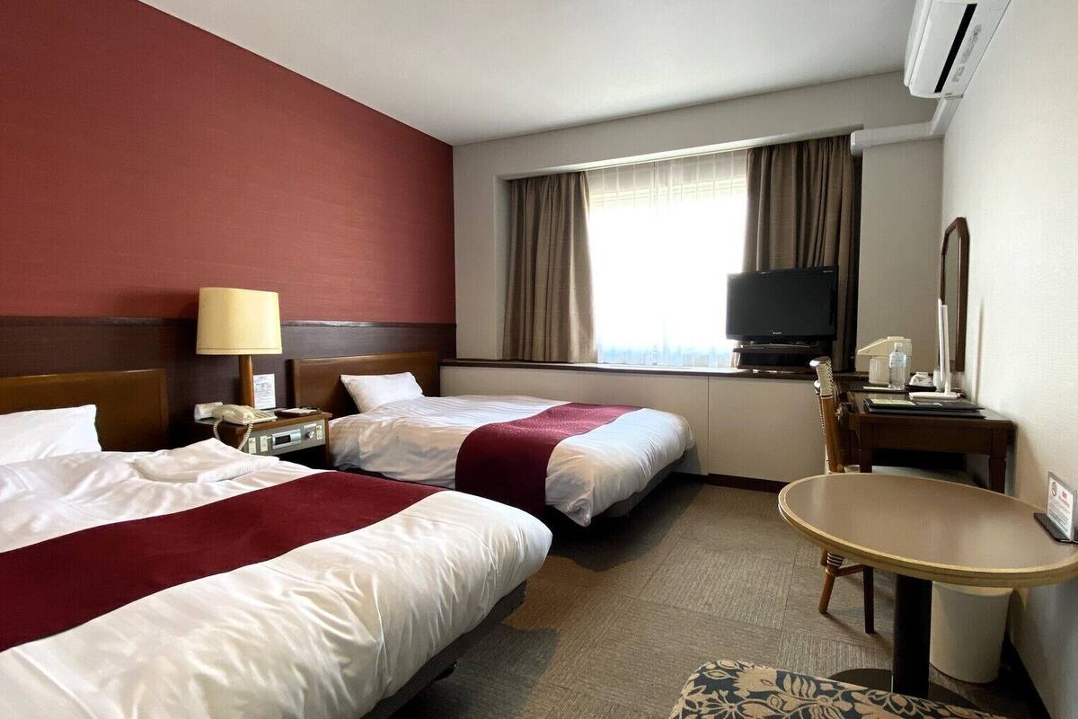 Quarto de hotel com duas camas, televisão, escrivaninha e banheiro.
