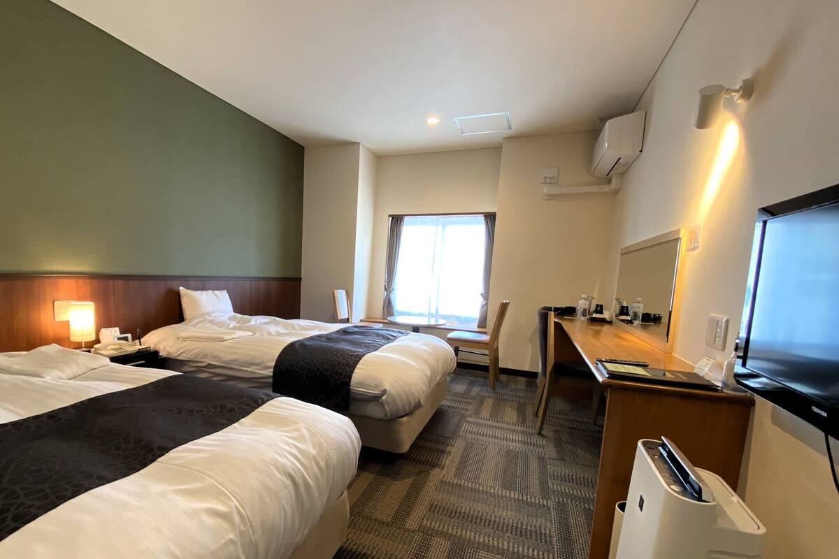 Quarto de hotel com duas camas, uma mesa, televisão e janela.