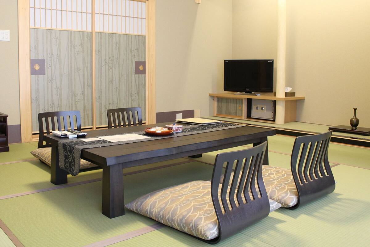 Quarto tradicional japonês com tatame, uma mesa baixa com almofadas, televisão e um armário com cofre.