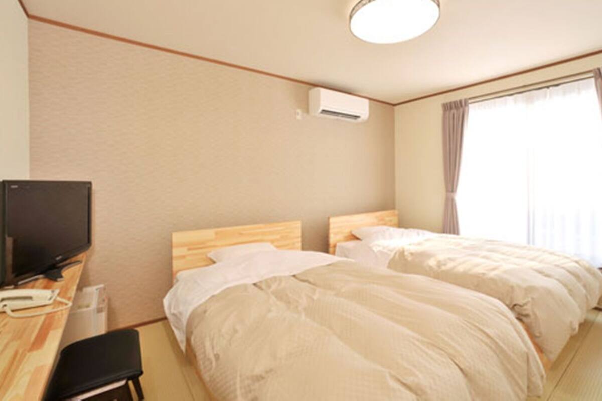 Quarto de hotel com duas camas, uma escrivaninha com televisão e um ar condicionado.