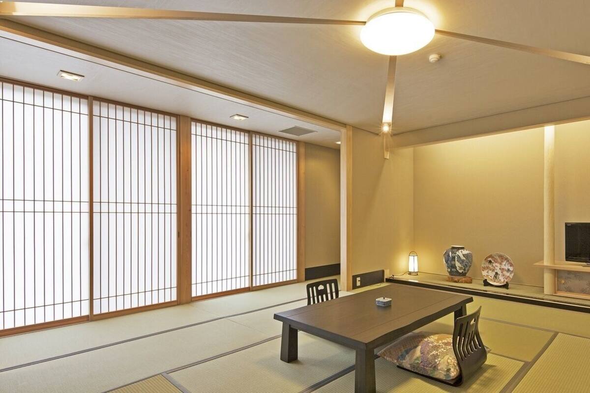 Um quarto japonês tradicional com tatames, uma mesa baixa, portas deslizantes, uma televisão e um ventilador de teto.