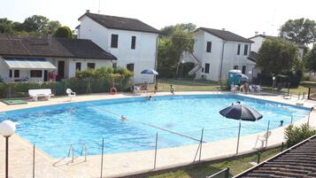 Piscina com deck ladrilhado, cercada por edifícios brancos com telhados escuros.