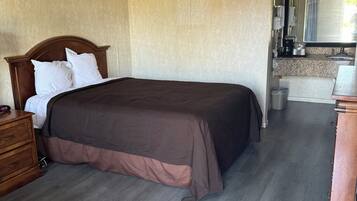 Quarto com cama grande, cabeceira de madeira e cómoda. Há uma pequena escrivaninha e um espelho no canto.