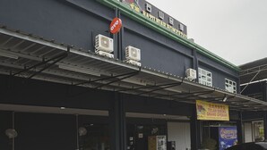Um edifício com placas 'Home' e 'Rashtriya Marine Products'. Há unidades de ar condicionado no telhado e uma placa 'Telah Dibuka' indicando que o estabelecimento está aberto.
