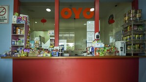 Uma loja bem iluminada com um grande letreiro 'OYO', prateleiras repletas de lanches e bebidas, e decorações festivas.