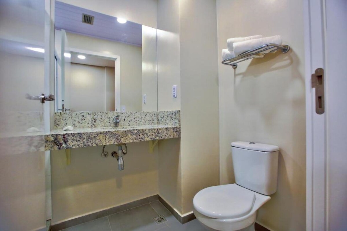 Um banheiro pequeno e moderno, com vaso sanitário branco, pia com bancada de granito e um espelho acima.