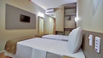 Quarto de hotel com duas camas, uma TV de tela plana na parede, aparelho de ar condicionado e um pequeno nicho com gancho.