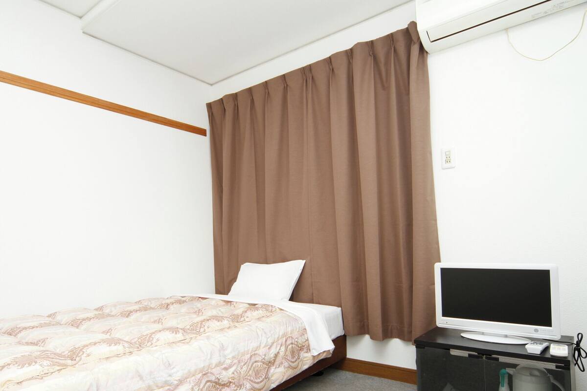 Quarto de hotel com cama, televisão e janela com cortinas marrons.
