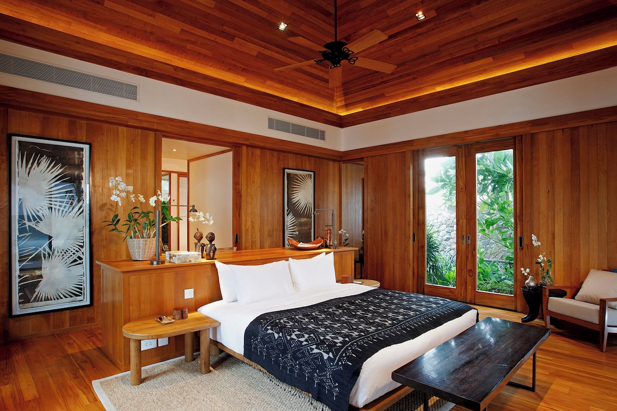 Quarto espaçoso com uma cama grande, teto de madeira e vista para o verde pela janela.