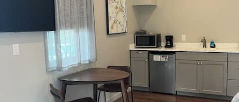 Cozinha moderna com micro-ondas, cafeteira e máquina de lavar louça. Uma mesa de jantar com cadeiras está localizada na sala de estar.