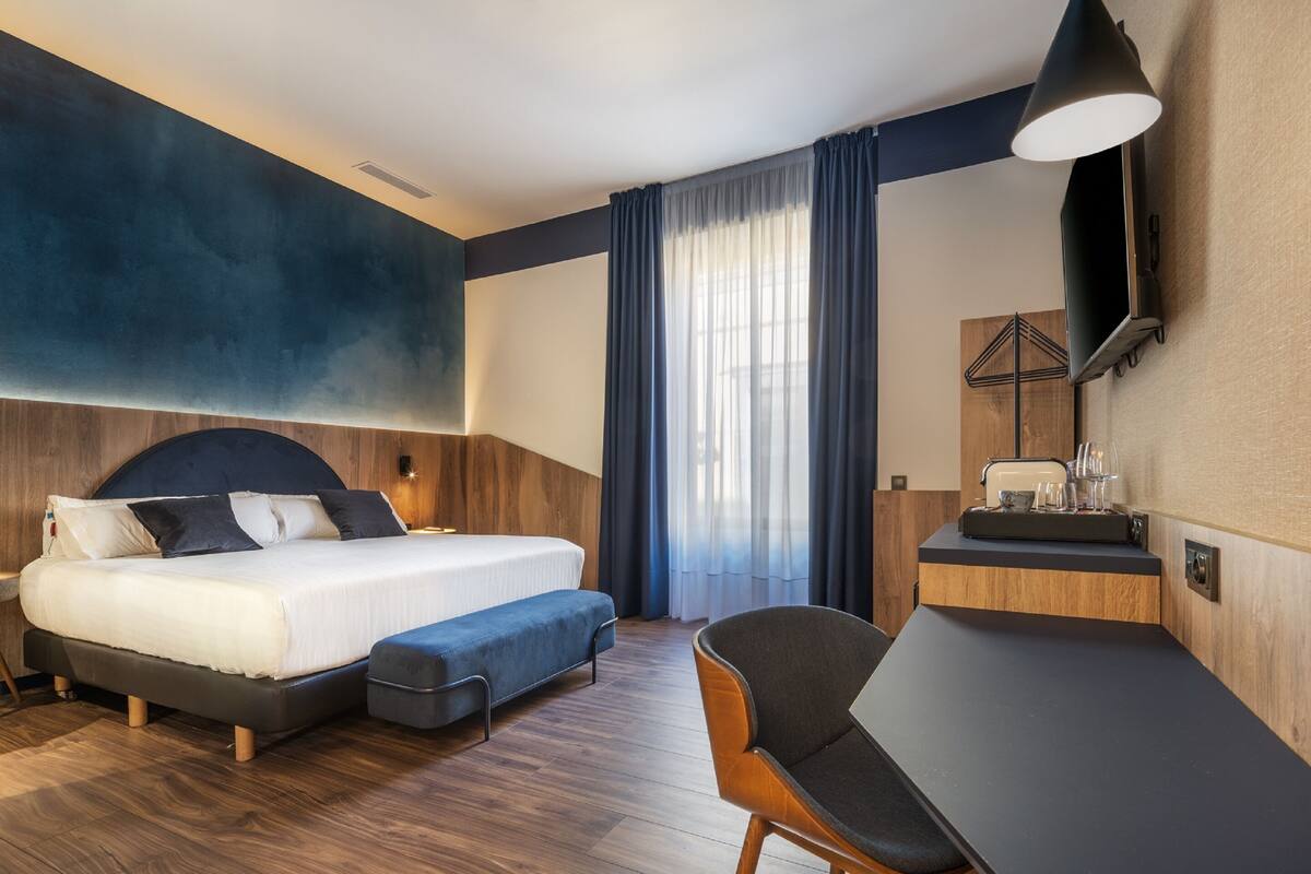 Quarto de hotel moderno com uma cama grande, uma escrivaninha e uma TV fixada na parede.