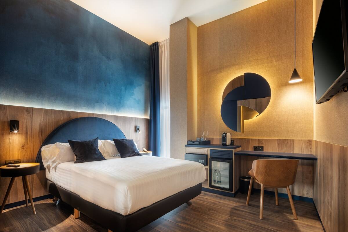 Quarto de hotel moderno com uma cama grande, uma escrivaninha, uma cadeira e uma televisão.